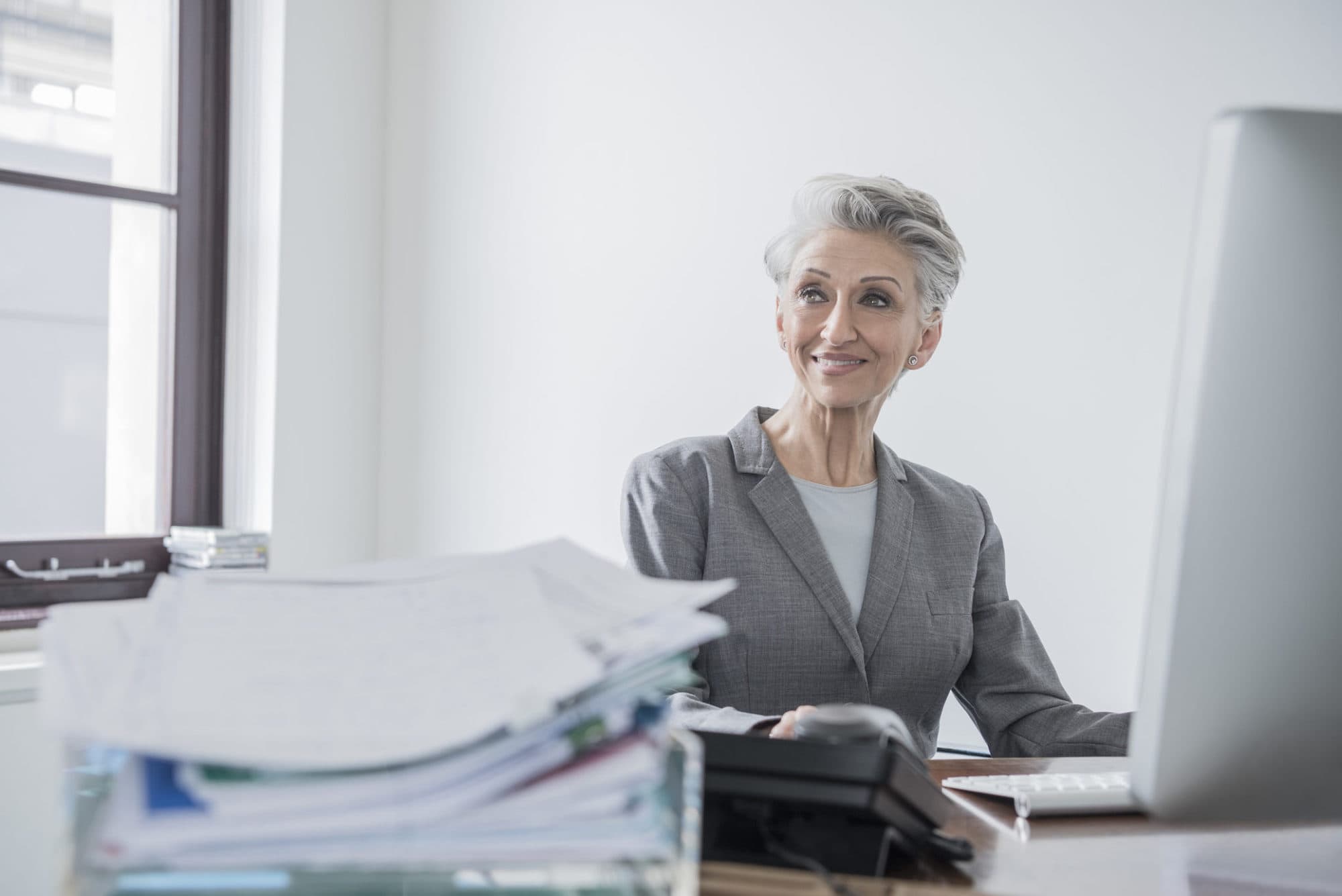 Mature office worker at desk looking away, smiling